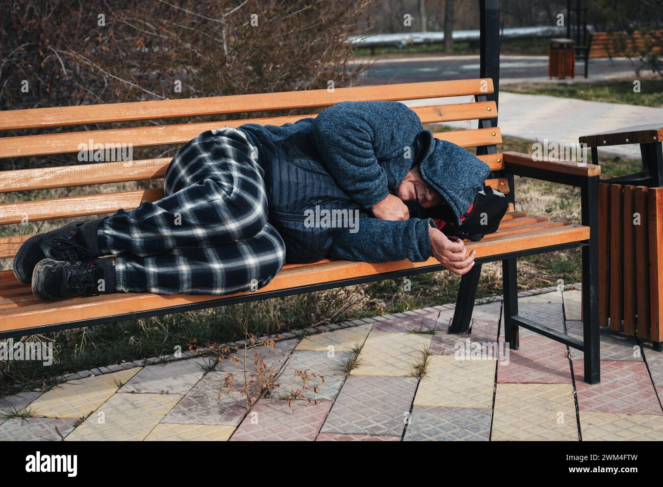homeless dirty elderly old Caucasian man lies sleeping on a park bench ...
