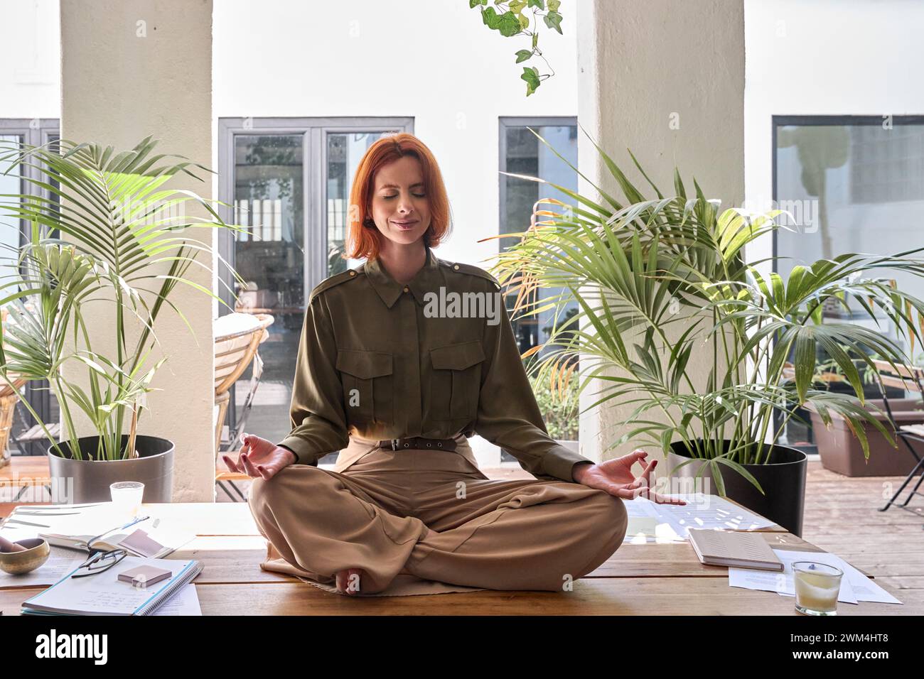 Calm happy young business woman sitting on work desk meditating ...