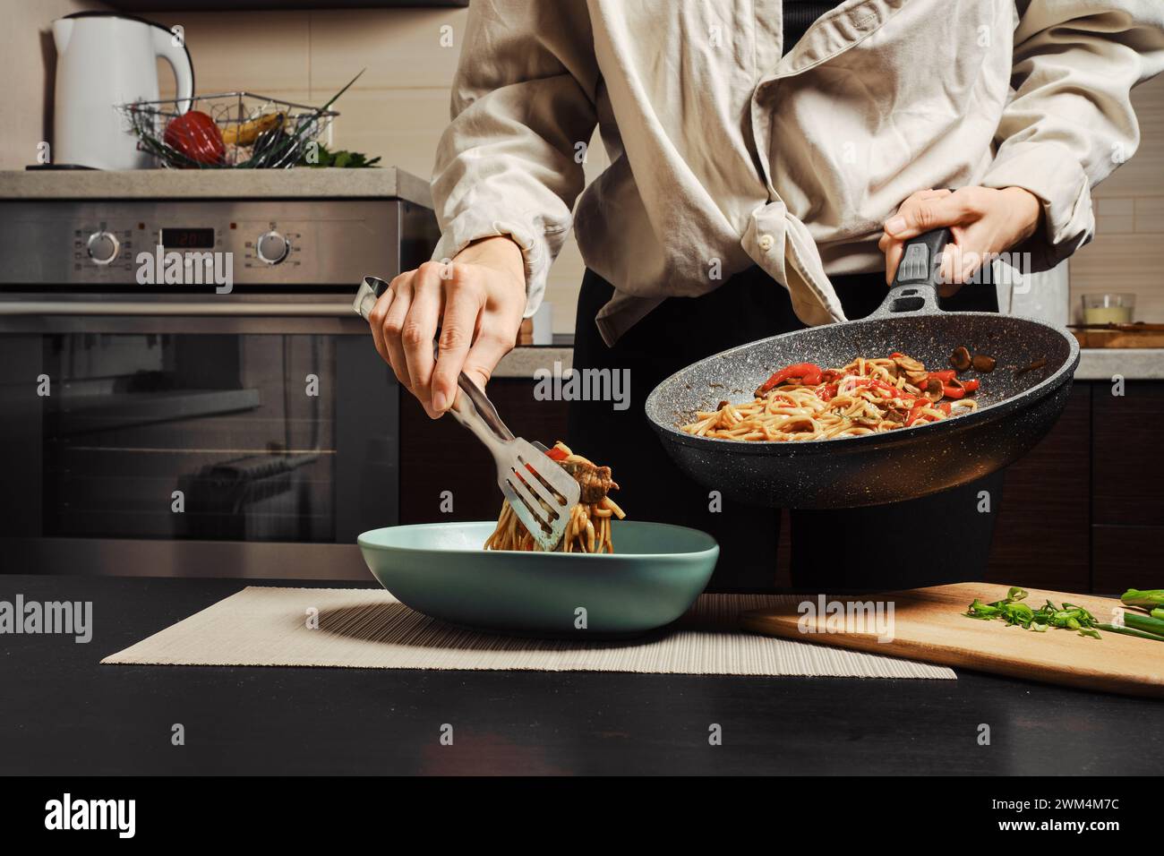 Unrecognizable woman moving cooked noodles with vegetables and beef ...