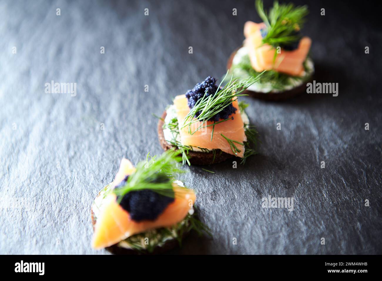 Smoked salmon canapes with cream cheese on black stone background ...