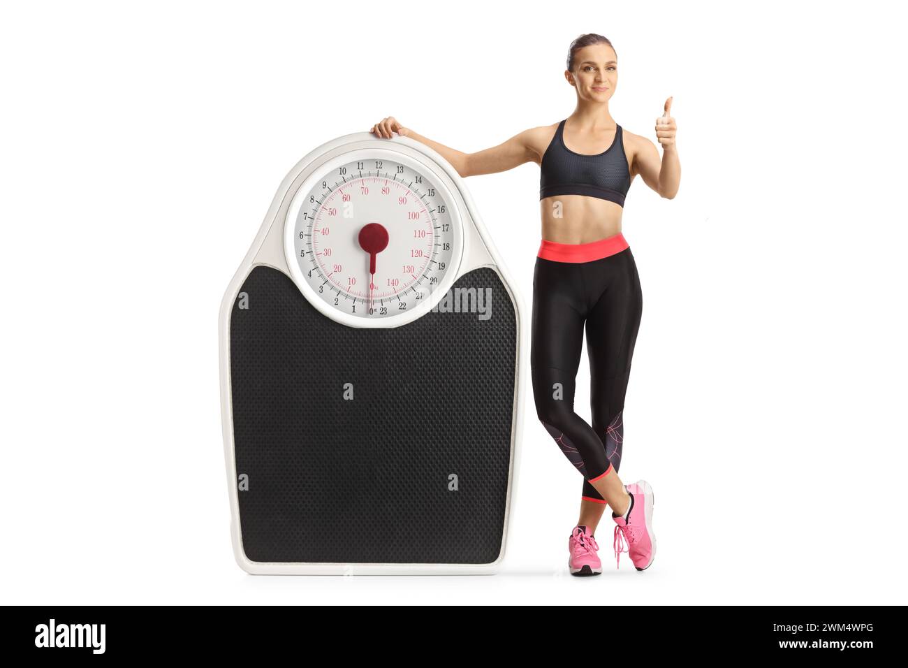 Fit young woman in sportswear gesturing thumbs up next to a big weight ...