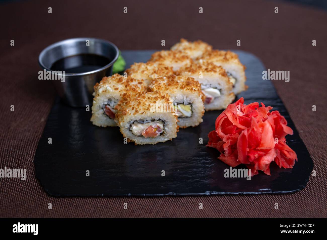 Deep-fried sushi roll on black stone plate with soy sauce, wasabi. Made ...
