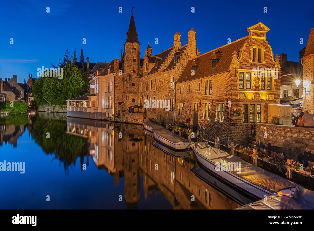 Evening atmosphere in Bruges at the Rosary Quay canal. Illuminated historic buildings of the old ...