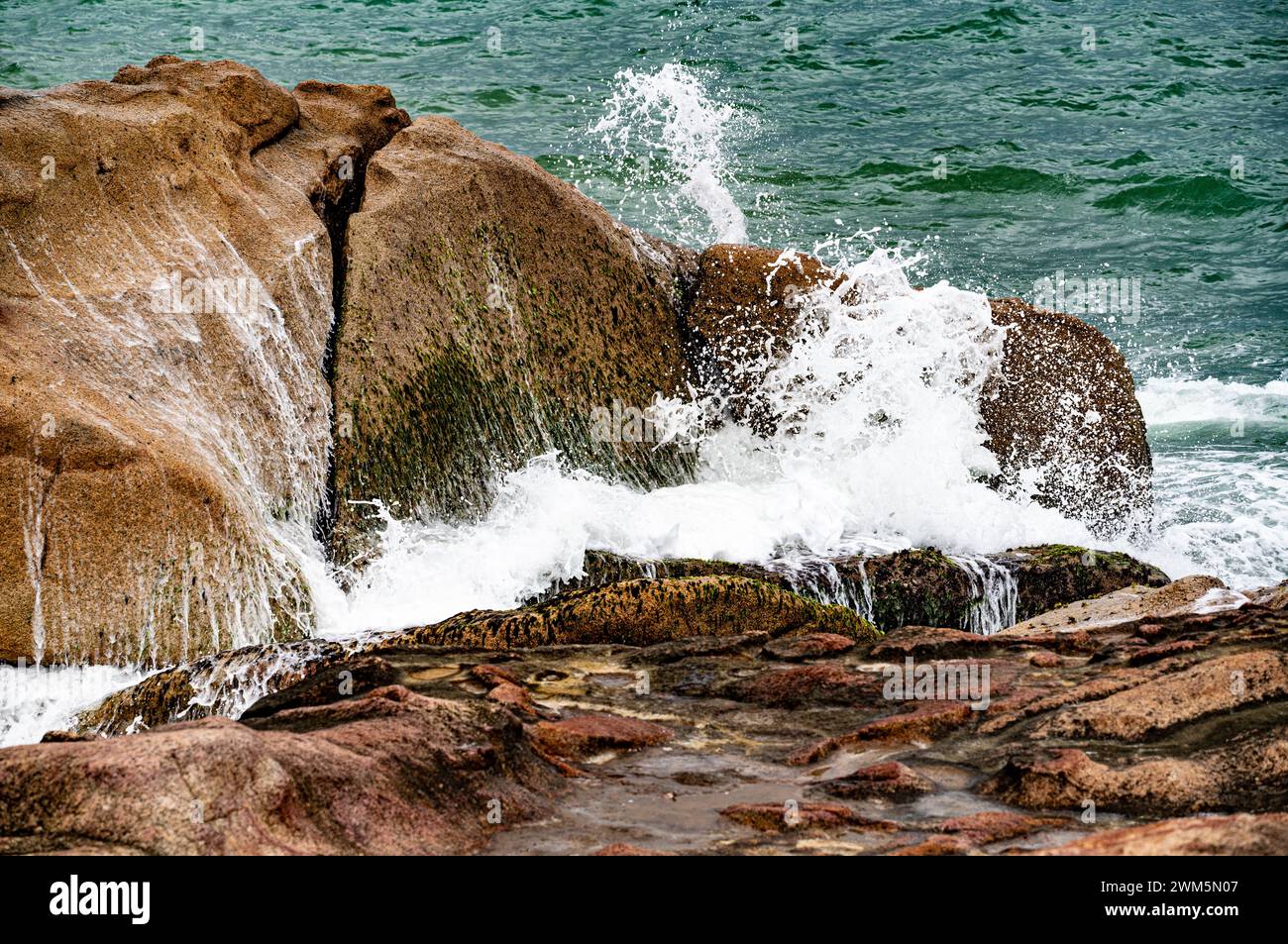 powerful waves relentlessly crash against rugged boulders and stones. sending salty spray into ...