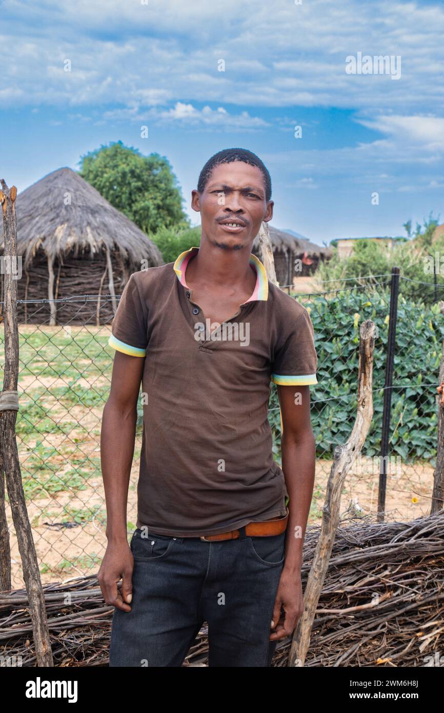 village african man standing in the yard, in the background hut with ...