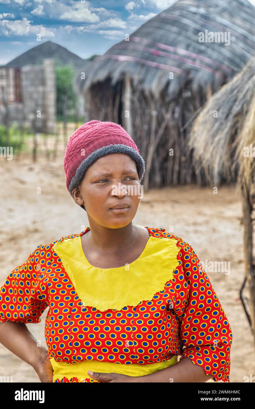 village african woman standing in the yard, in the background hut with thatched roof, in south ...