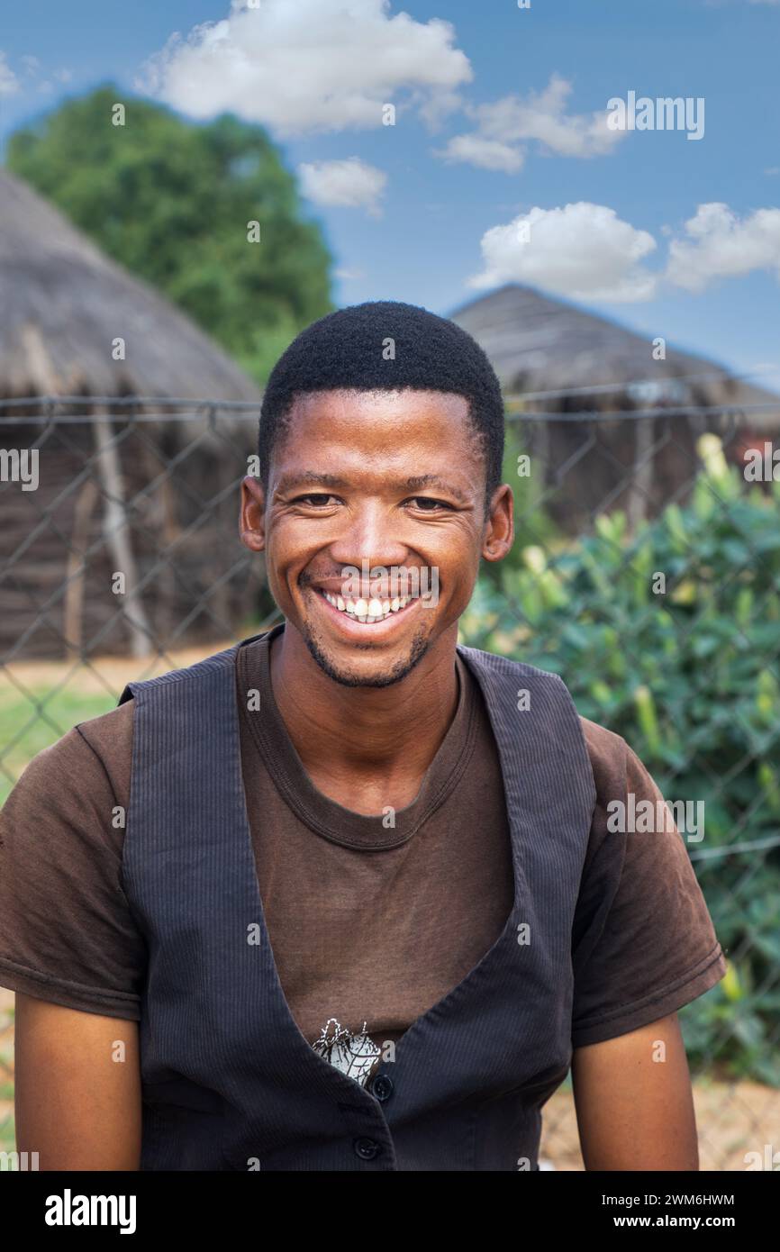 village african man standing in the yard, in the background hut with thatched roof, in south ...