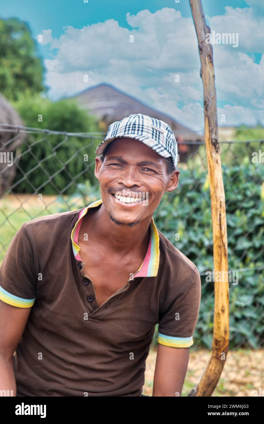 village african man standing in the yard, in the background hut with ...