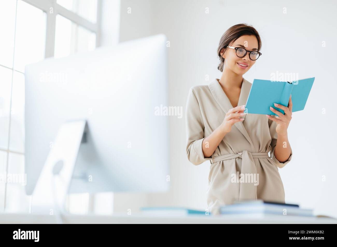 Cheerful, smartly dressed businesswoman holding a book, looking ready ...