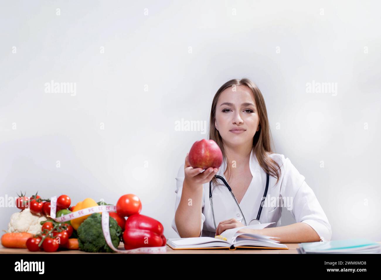 Smiling nutritionist in her office, she is showing healthy vegetables ...