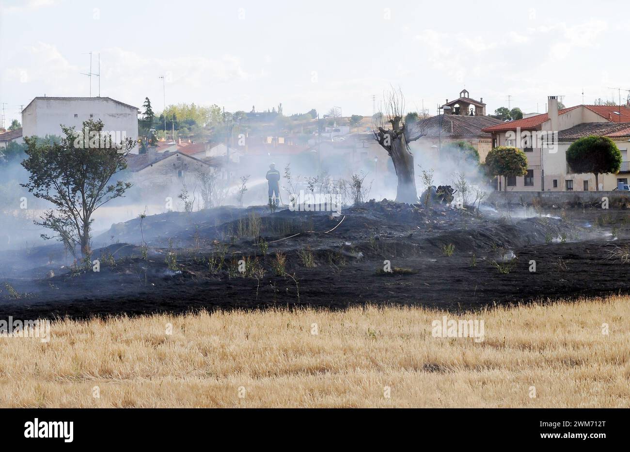 Firefighter through the smoke cooling the burned grass with water after ...