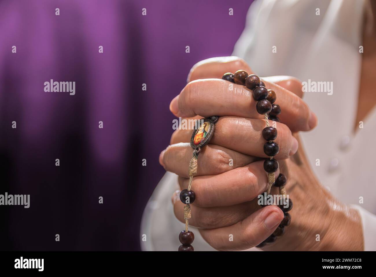close up of adult woman using the rosary in front of a violet ...