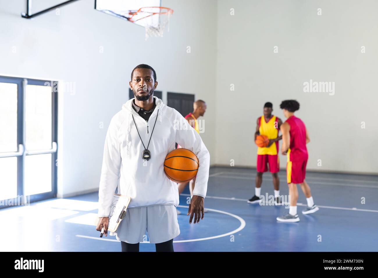 An African American coach stands confidently in a gym, holding a ...