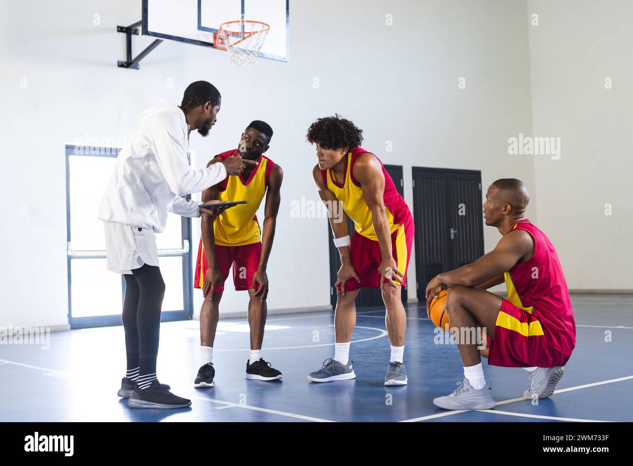 African American coach strategizing with basketball players indoors ...