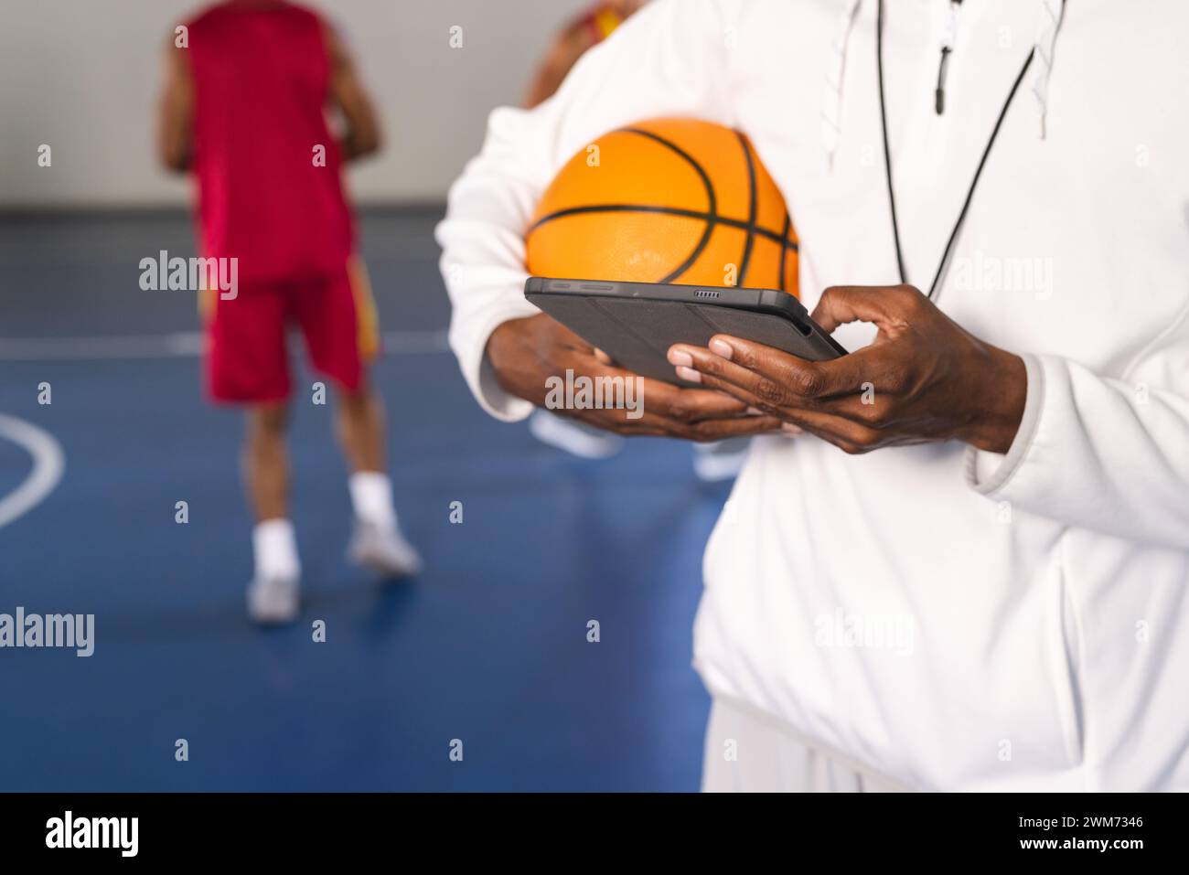 African American coach holds a basketball and uses a tablet, with copy ...