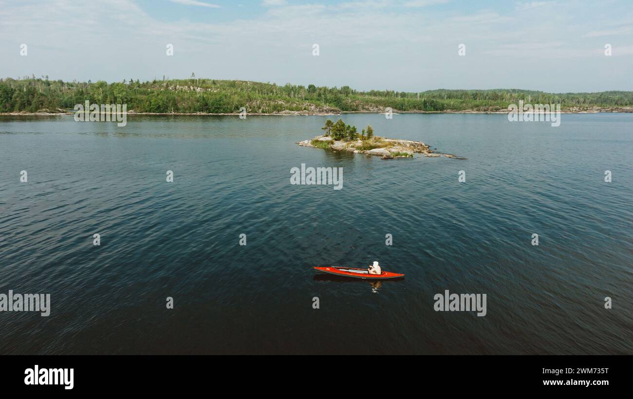 A lone kayaker in a red vessel glides through the water near a small ...