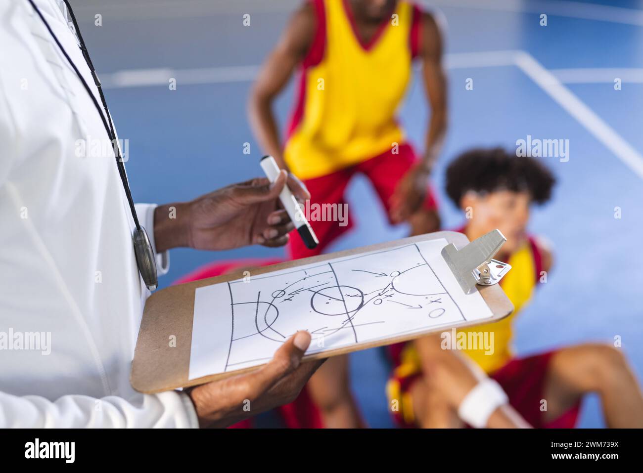 Coach outlines strategy on clipboard at indoor basketball court ...