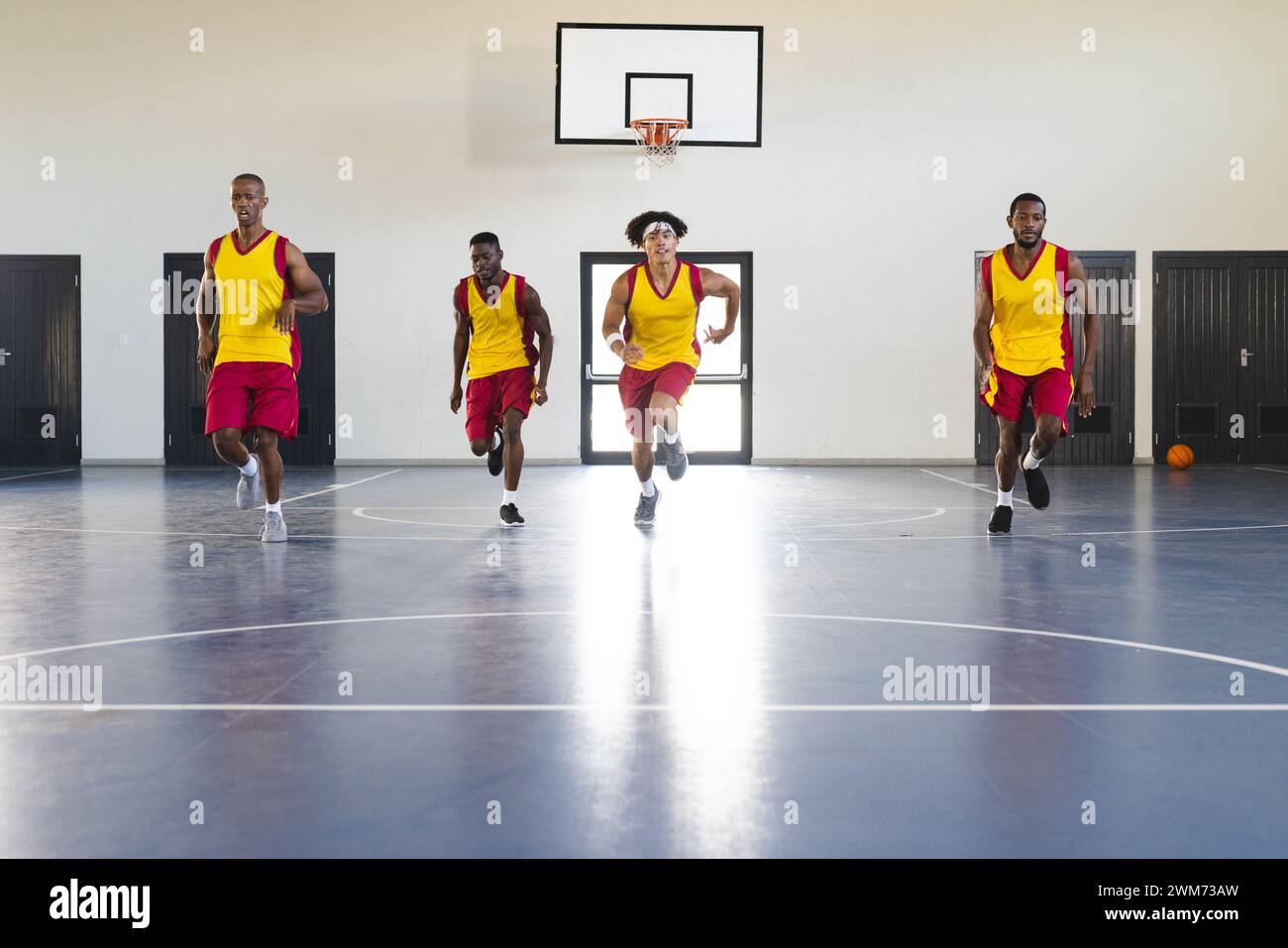Diverse basketball players sprint across an indoor court with copy ...