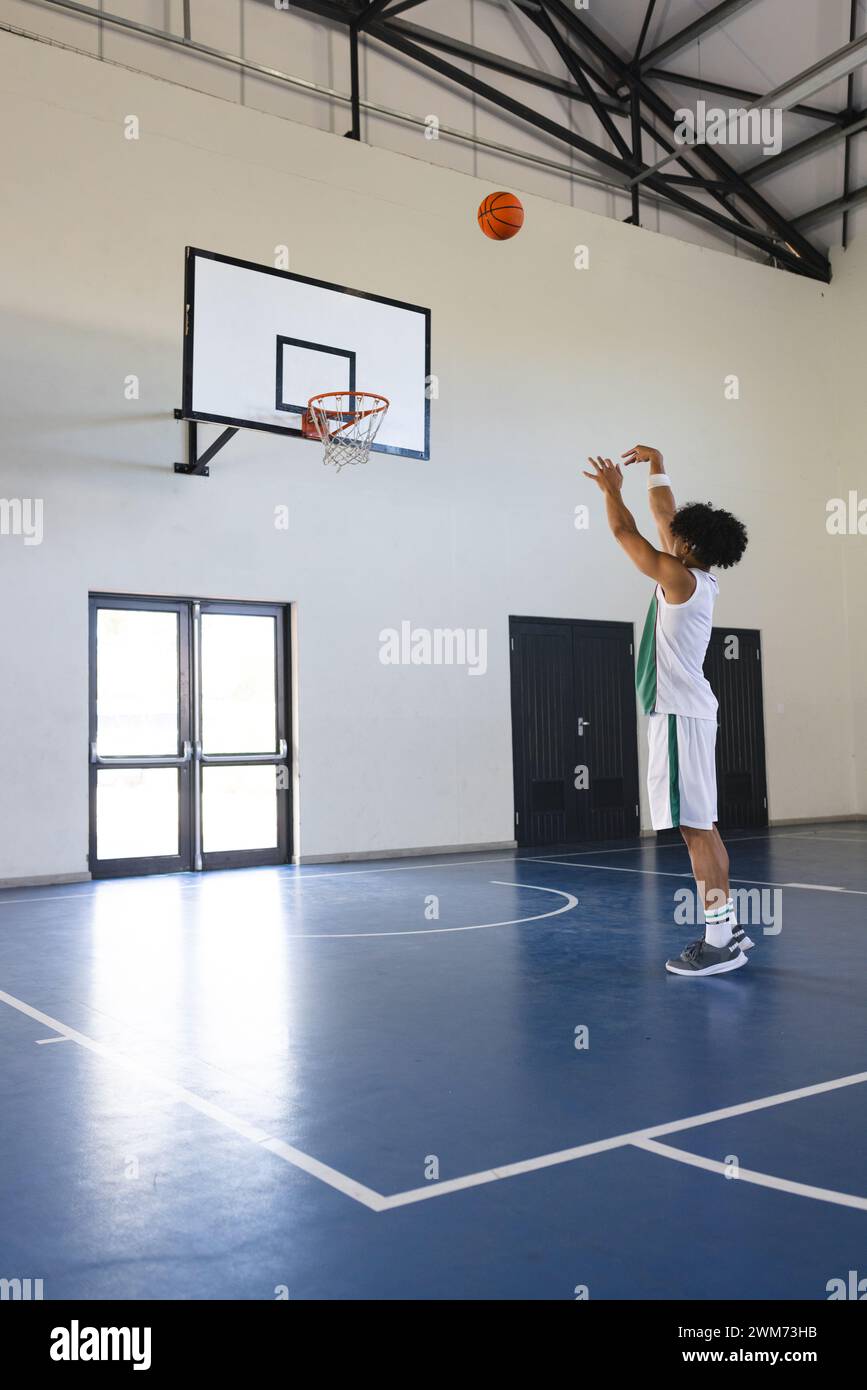 Young biracial man practices shooting a basketball in a gym with copy ...