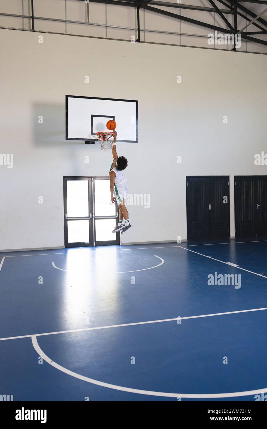 An athlete performs a jump shot in an indoor basketball court with copy ...