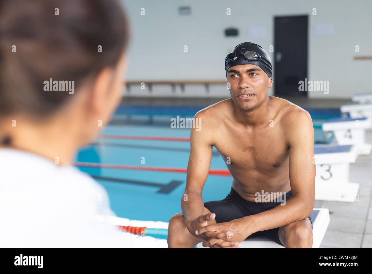 Young biracial male athlete swimmer listens intently at the poolside ...