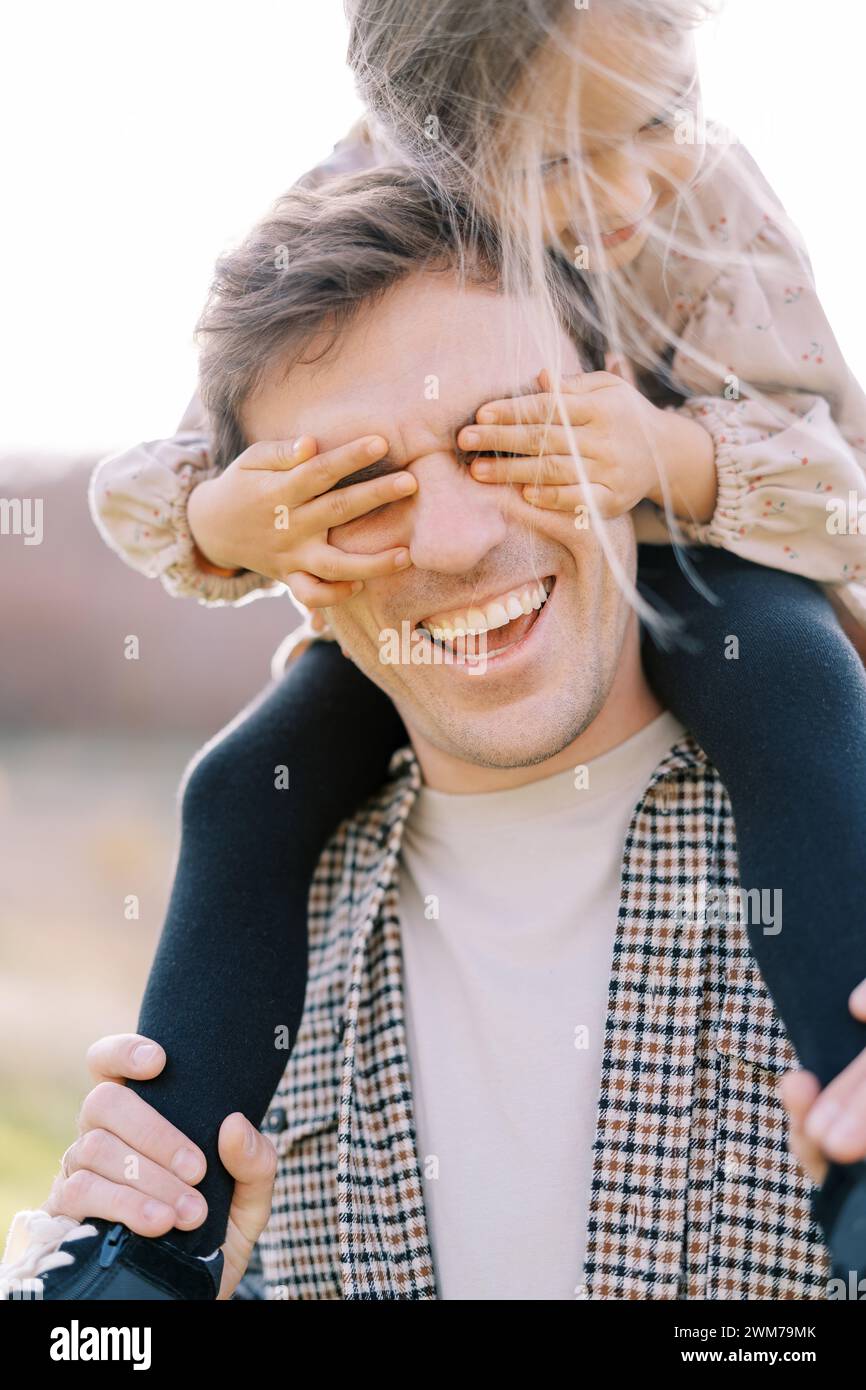 Little girl covered her laughing dad eyes with her palms while sitting ...