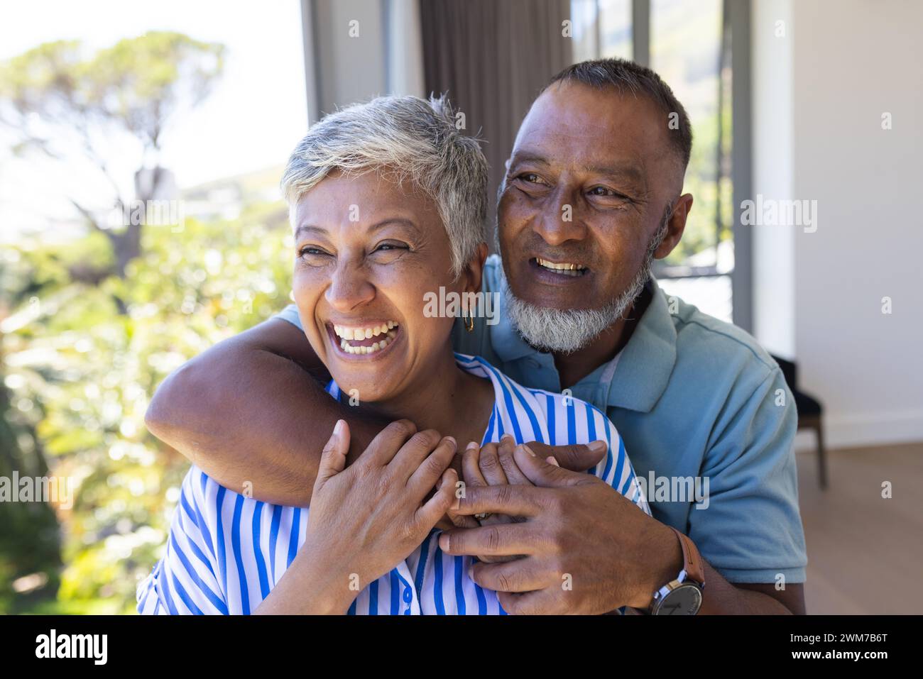 Senior biracial couple shares a joyful embrace at home. Their laughter ...