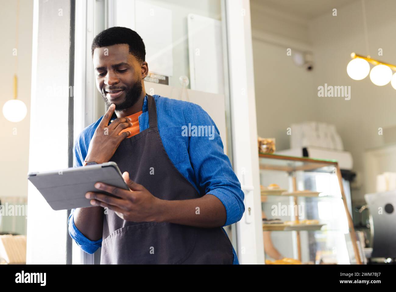 African American man reviews inventory on a tablet at a bakery, with ...