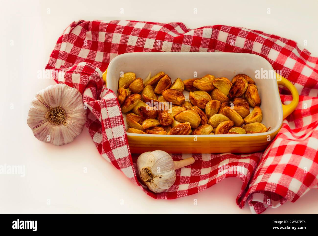 baked garlic cloves in the dish placed on teat owel in a red white ...