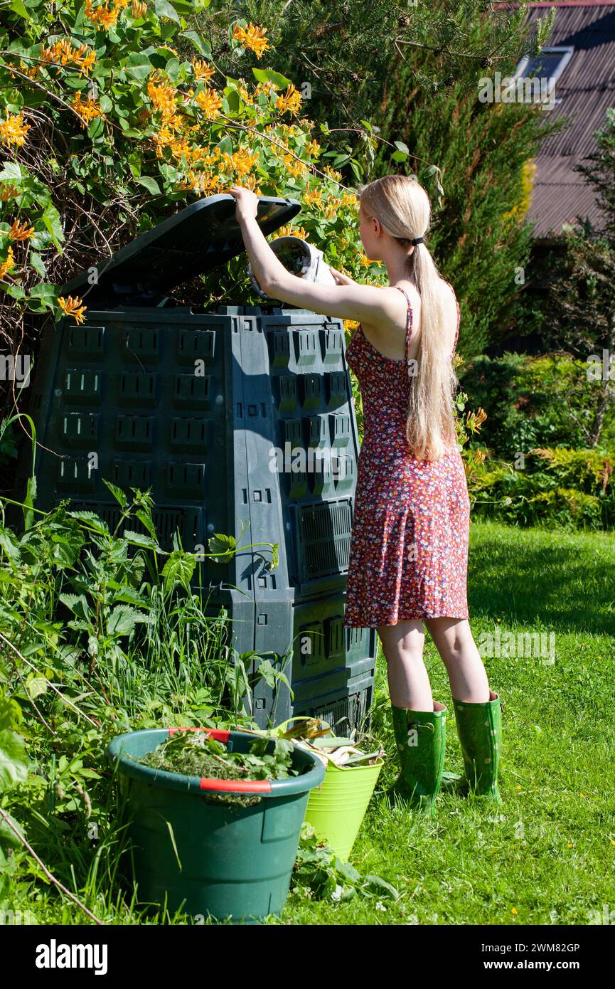 A young girl puts vegetable waste into a compost bin in the garden in ...