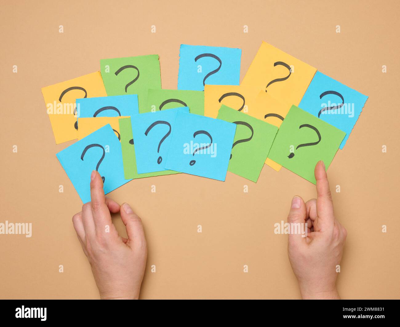 Female hands hold paper sheets with a drawn question mark on a beige ...