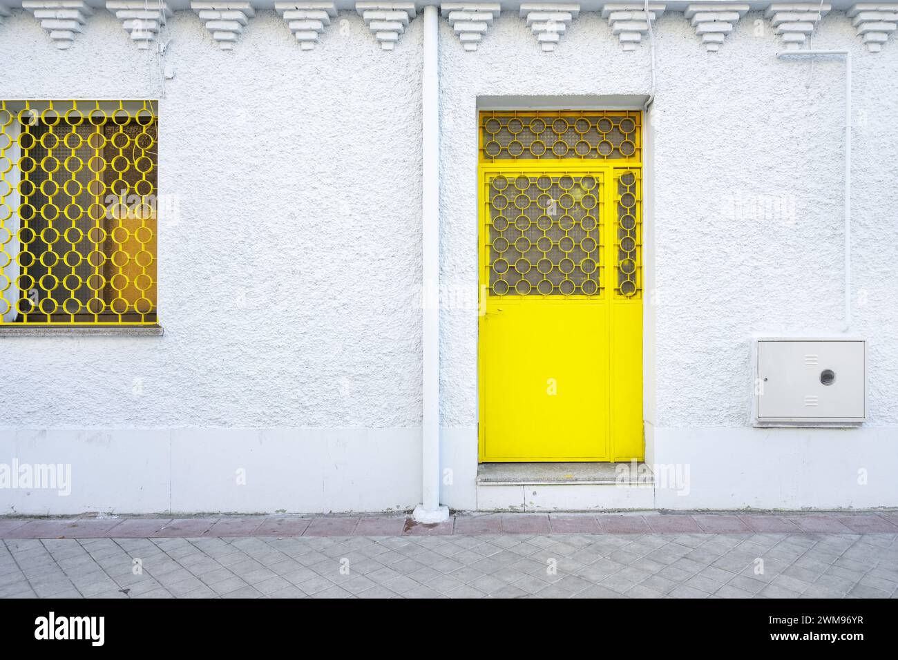 Yellow door with security lock and metal bars on the windows on a white ...