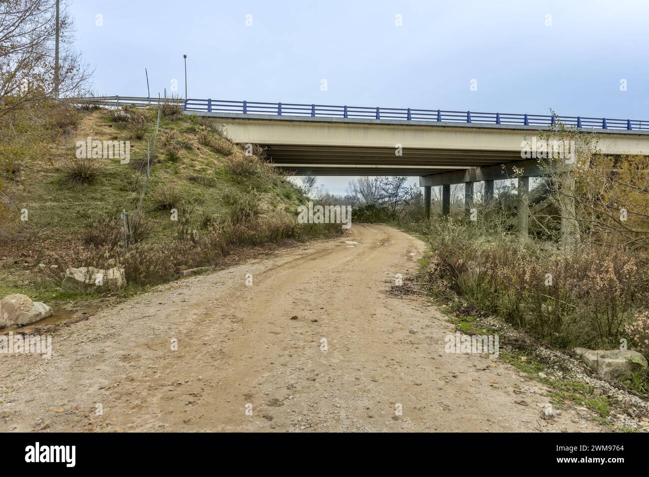 A dirt road passing under a highway bridge with two independent ...