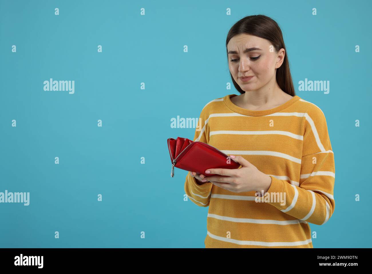 Sad woman with empty wallet on light blue background, space for text ...