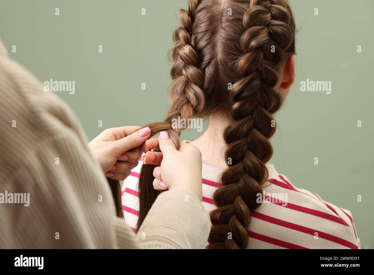 Professional stylist braiding woman's hair on olive background, closeup ...