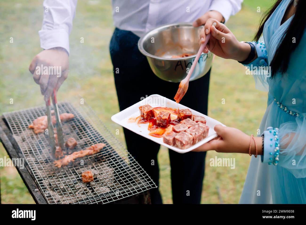 A couple grills some cutlets on a charcoal grill during spring. Garden ...