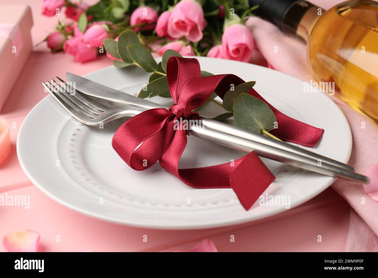 Romantic place setting. Plate, cutlery, eucalyptus branch and roses on ...