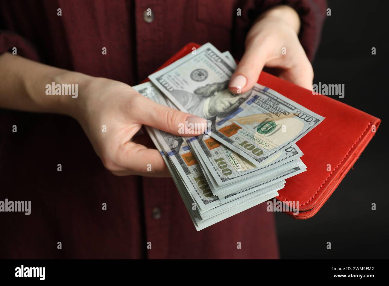 Money exchange. Woman putting dollar banknotes into wallet on dark ...