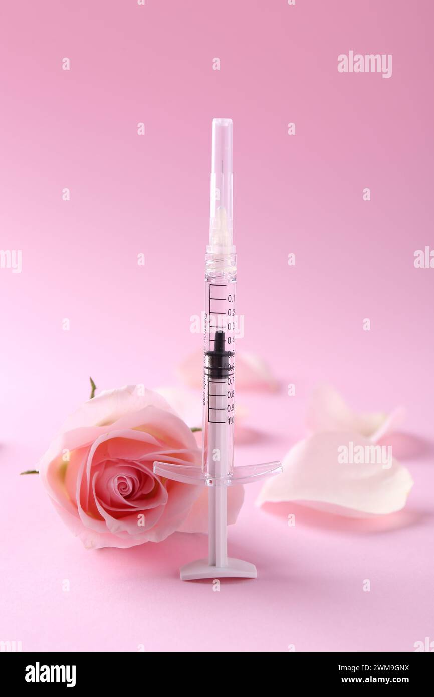 Cosmetology. Medical syringe, rose flower and petals on pink background ...