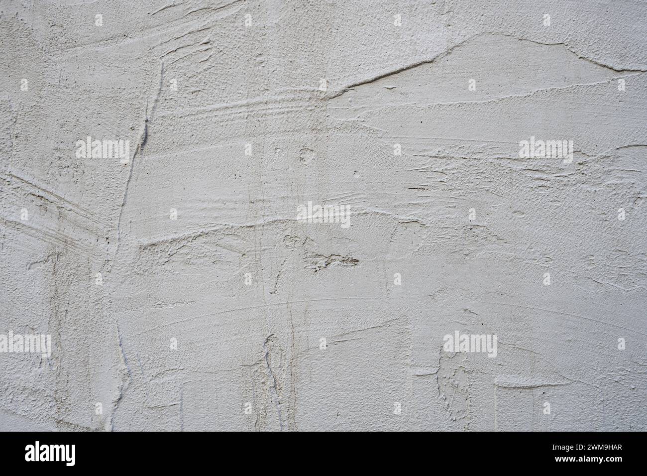 A gray cement wall with carelessly smoothed layers of white plaster and ...