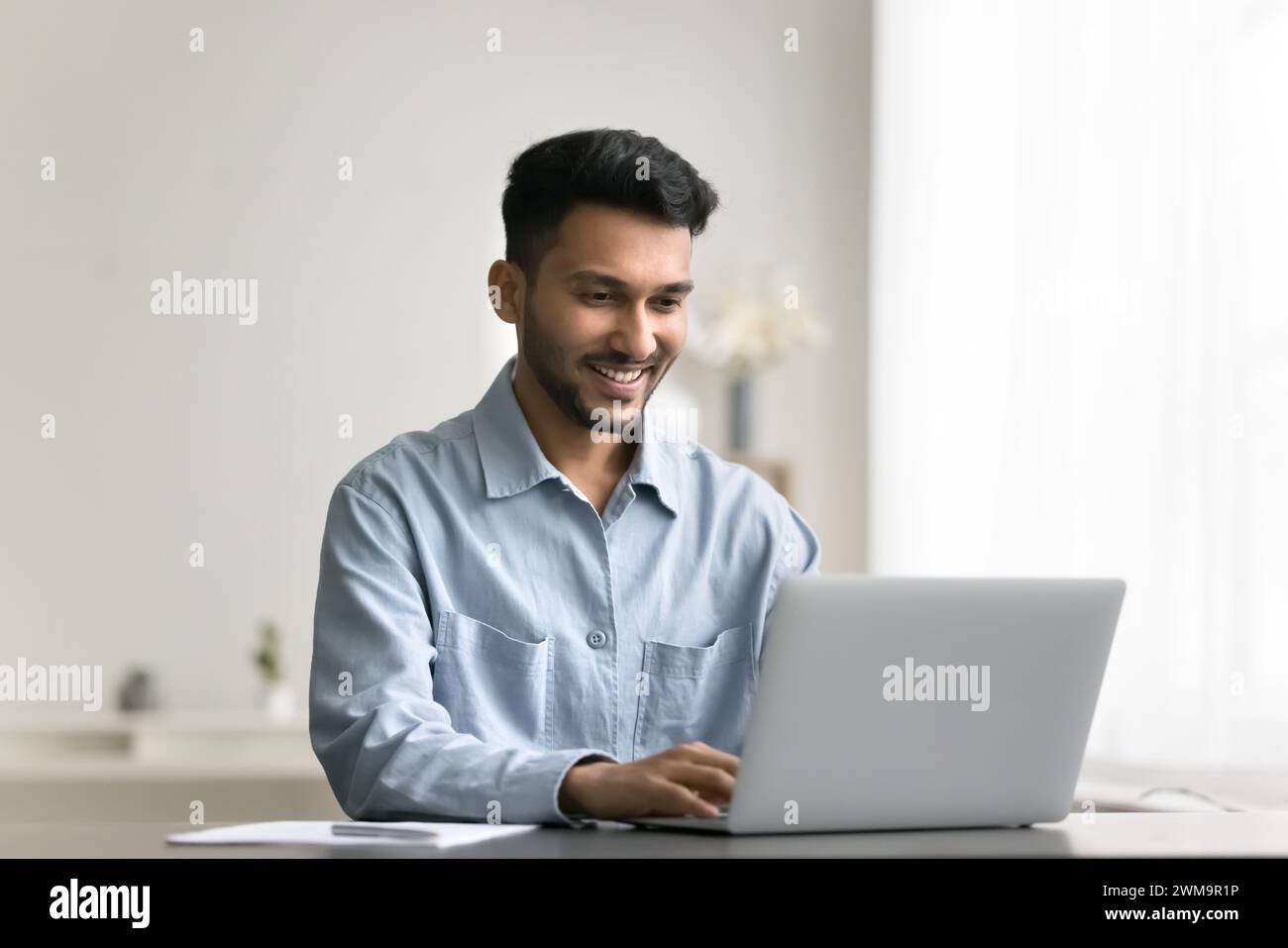 Smiling Indian man working or studying using modern wireless computer ...
