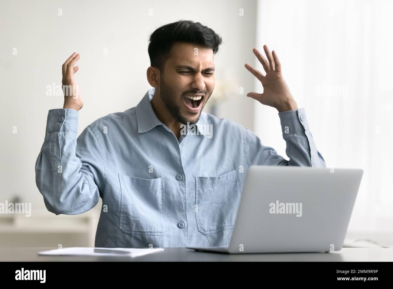 Indian man sit at desk looks at laptop screen and yelling Stock Photo ...