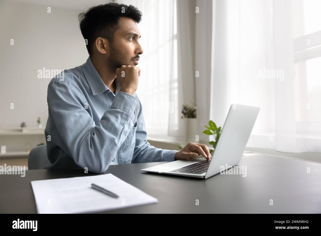 Distracted from laptop work pensive Indian man looking in distance ...