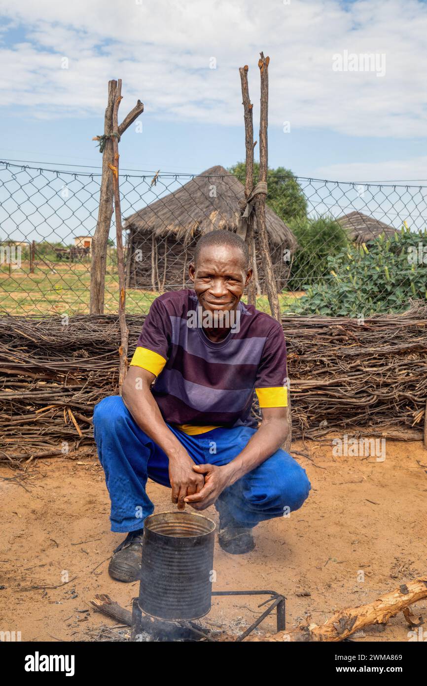 village african man in the yard, cooking in the outdoors kitchen, in the background hut with ...