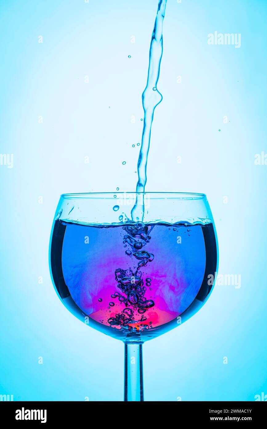 Pouring water into wine glass with red and blue liquid, illuminated in ...