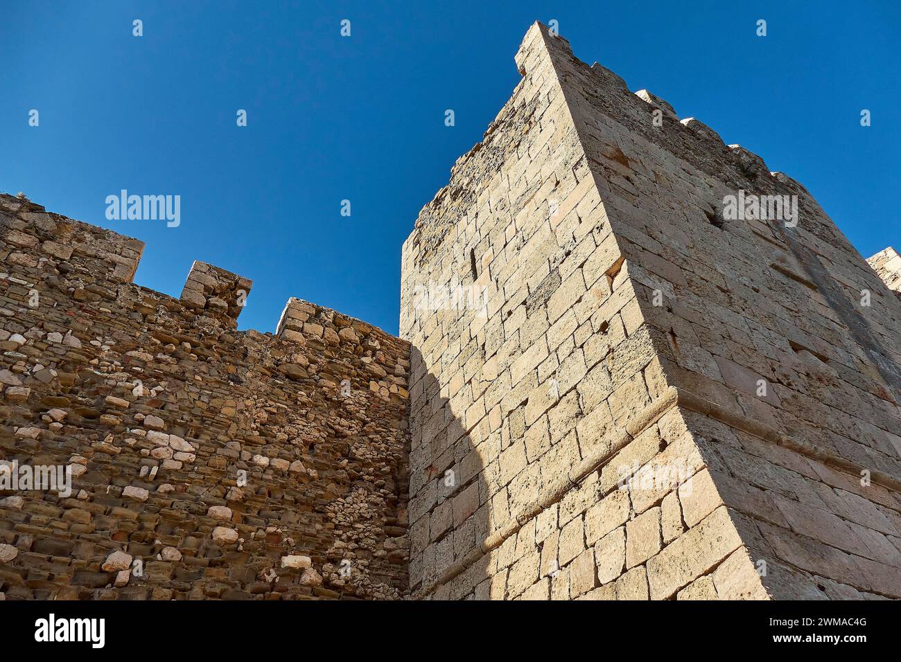 The sunlit wall of an old castle rises into the deep blue sky, sea ...