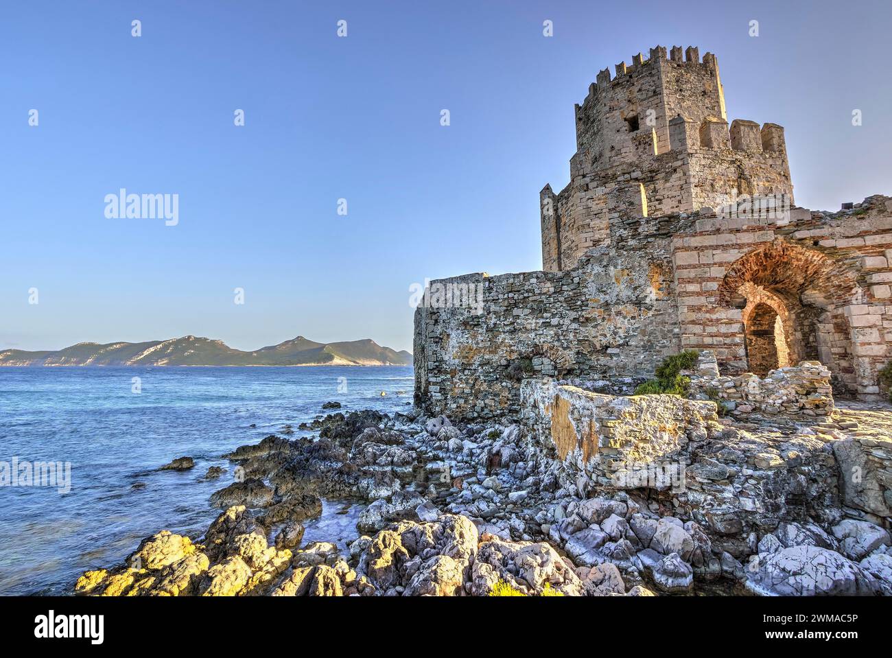HDR photo of an old castle on the coast with blue sky and mountains in ...