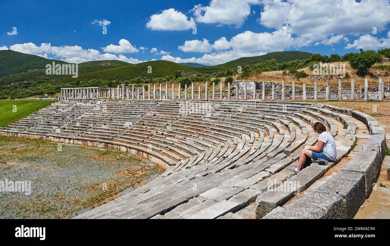 Person sitting in ancient stadium under clear blue sky with mountains ...