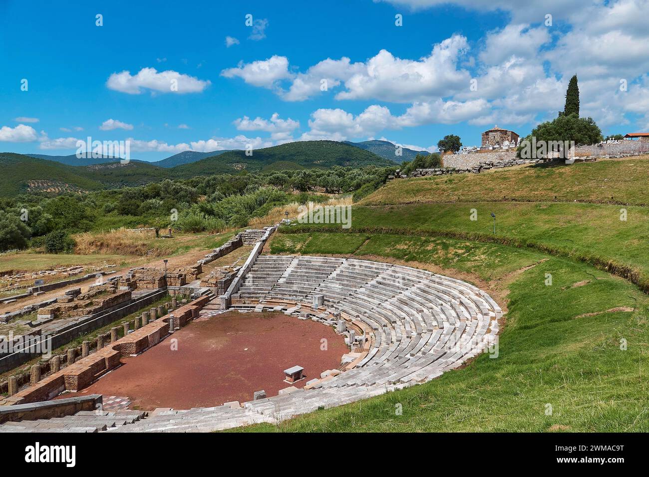 Ancient amphitheatre with rows of seats on a green meadow surrounded by ...