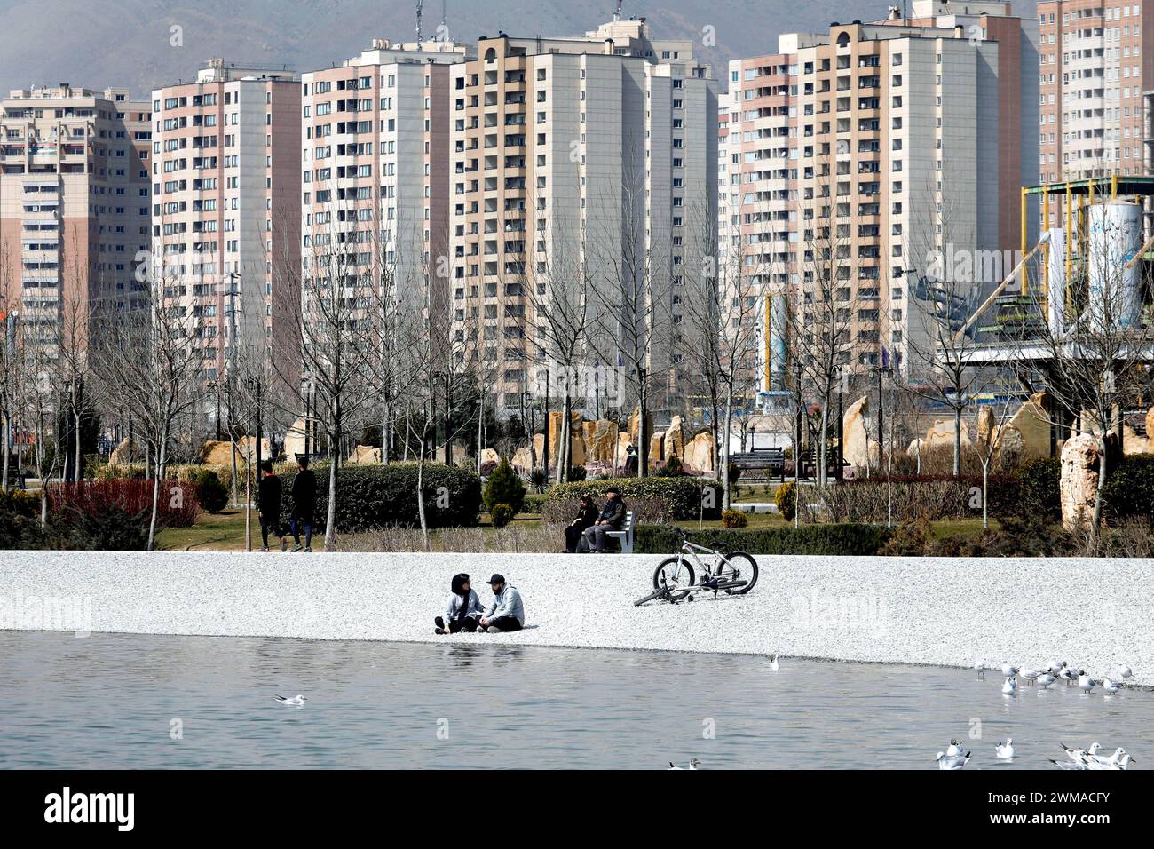 A young couple sits on the beach of Lake Chitgar in Tehran, Iran. Lake ...